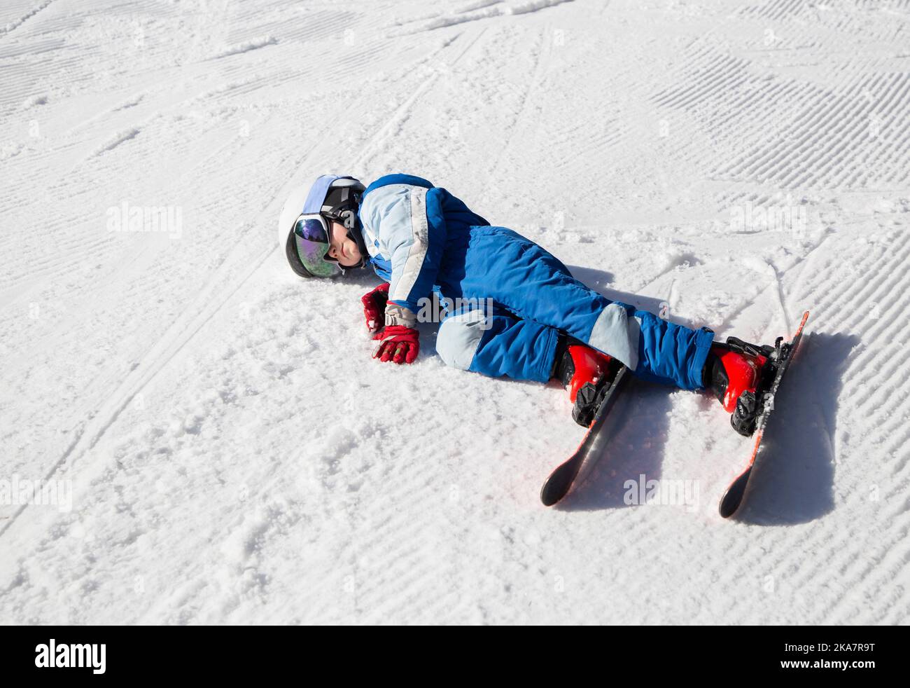 tired child in a helmet, glasses, skis and winter overalls lies on the ...
