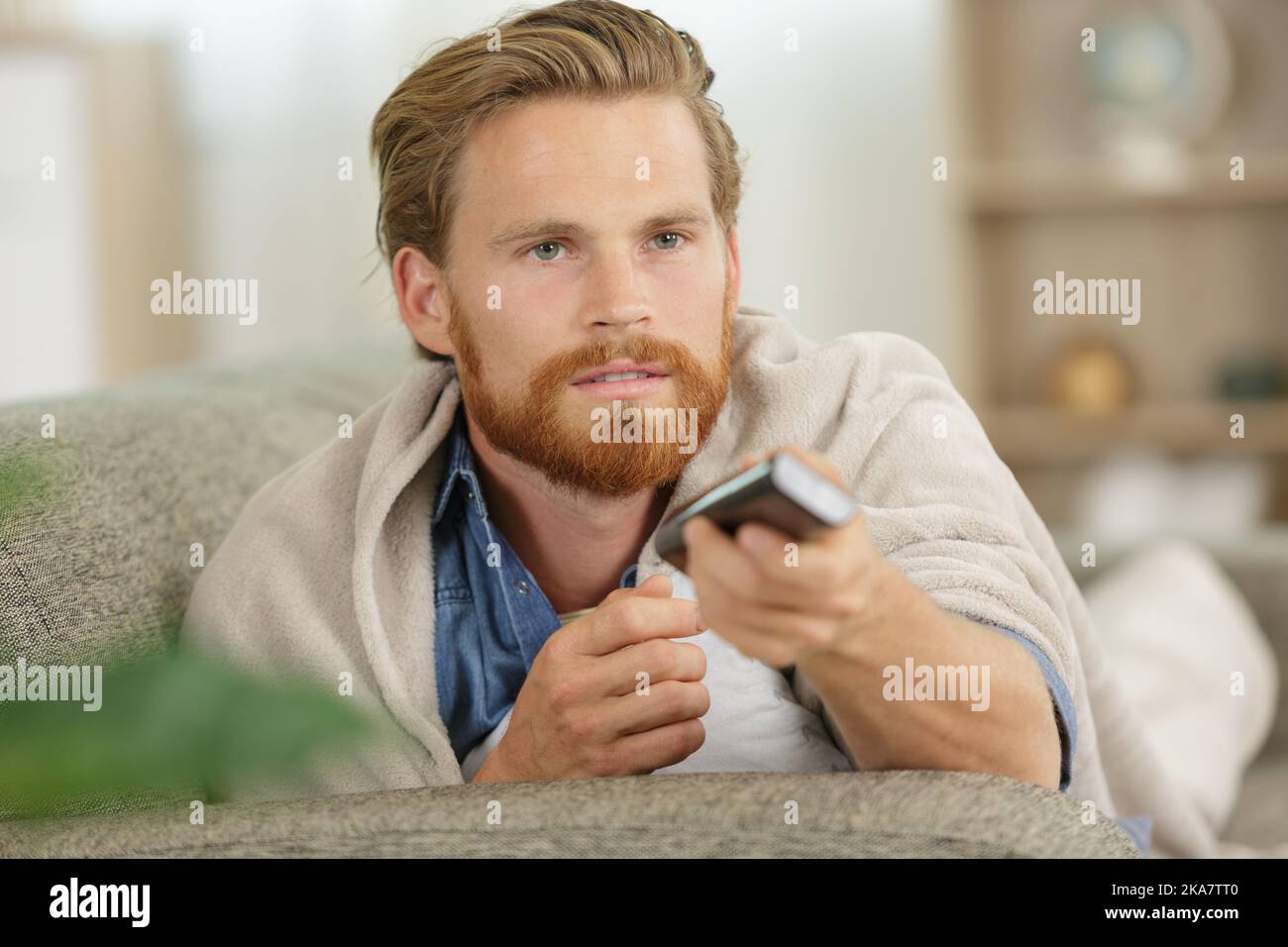man on sofa covered with blanket using remote control Stock Photo - Alamy