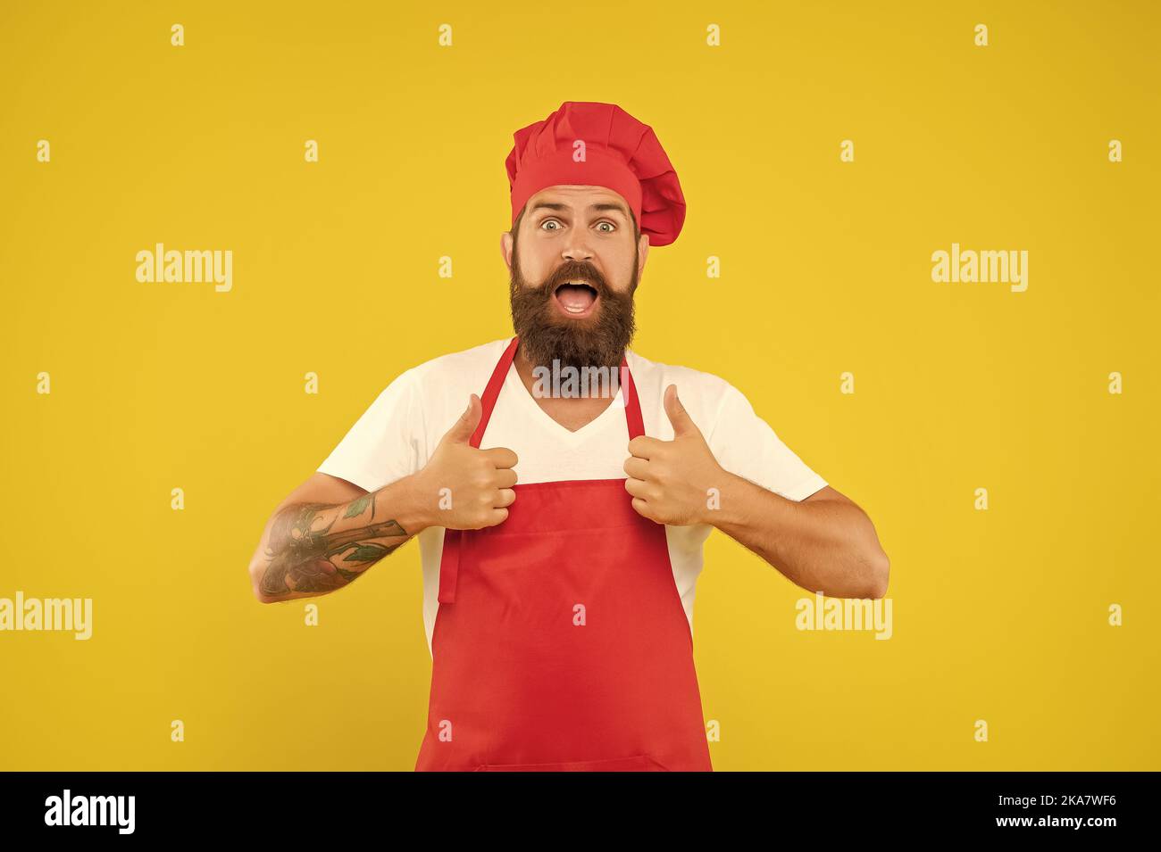 Surprised man in toque and apron giving double thumbs yellow background ...