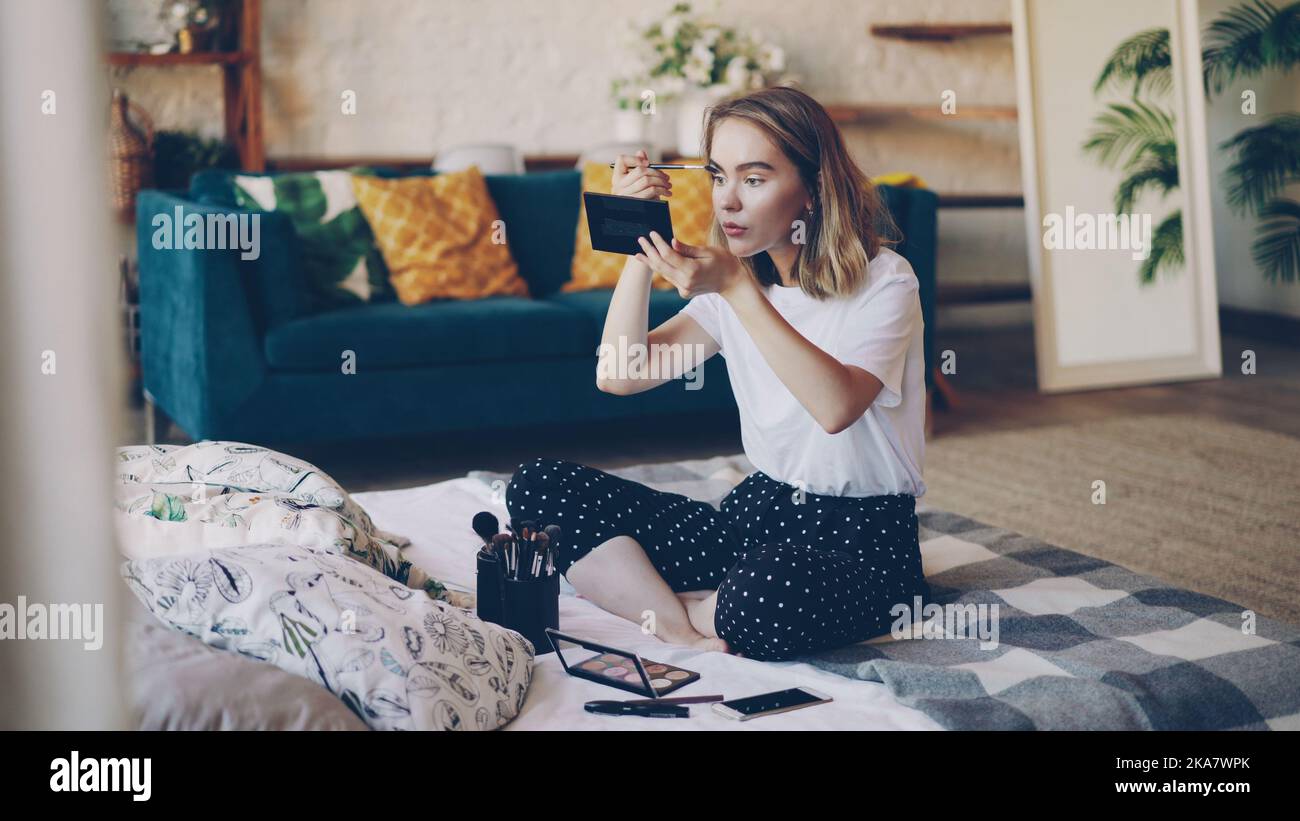 Beautiful blond girl is putting on makeup painting eyebrows with brush ...