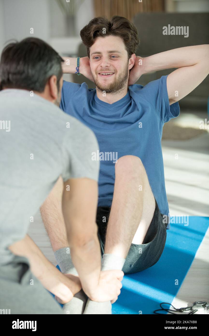 personal trainer holding feet while young man does sit ups Stock Photo ...
