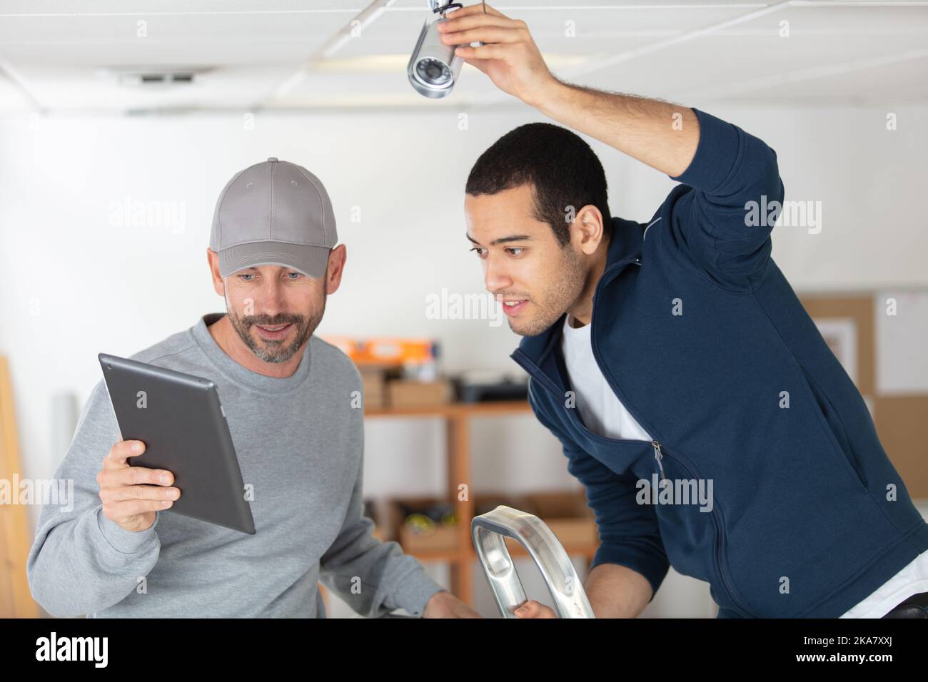 two male contractors working on cctv camera on ceiling Stock Photo - Alamy