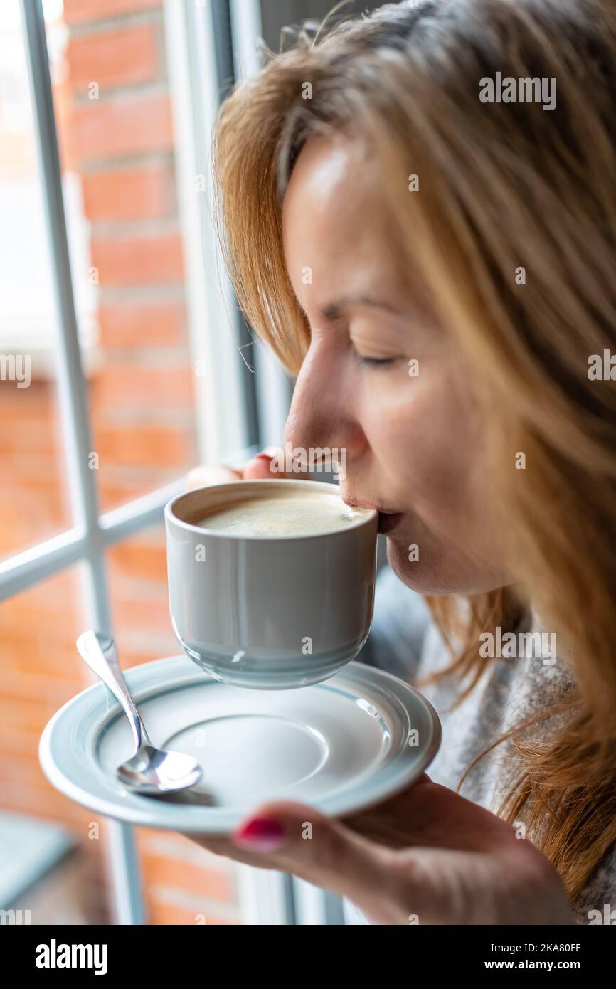 Woman holding a cup of coffee while taking a sip of the drink by the ...