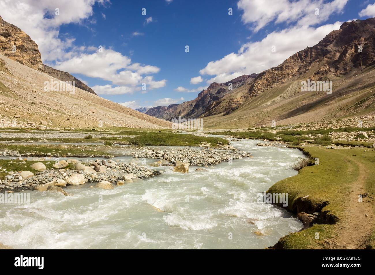 The Zanskar river flows through grassy meadows in the high Himalayan ...