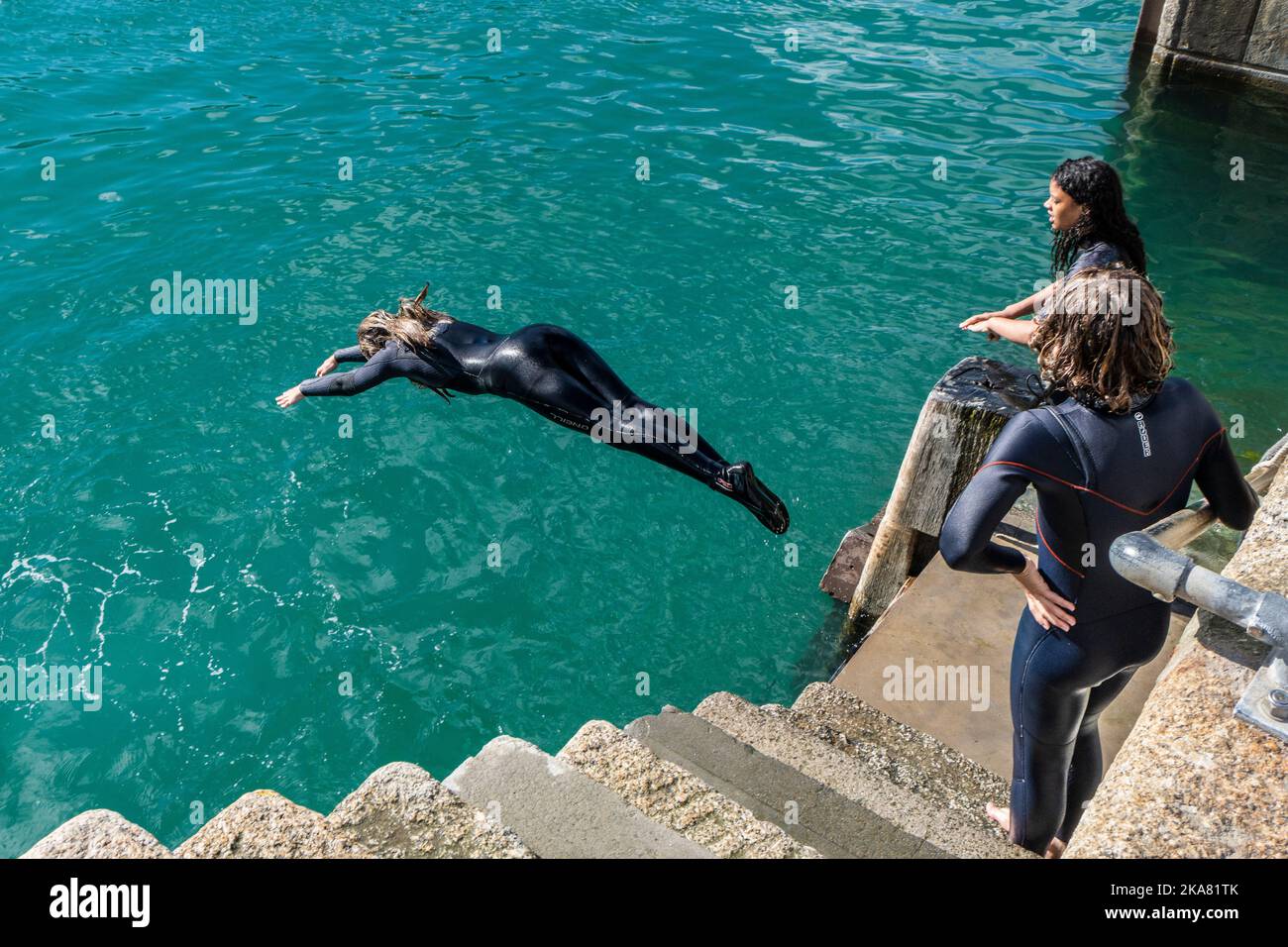 A young teenagers diving into the sea at high tide from the quay in ...
