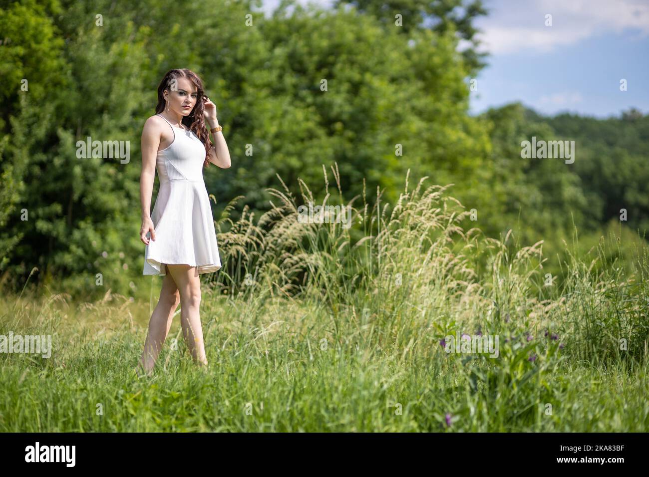 The Beautiful Girl In A White Summer Dress Posing In The Green Meadow