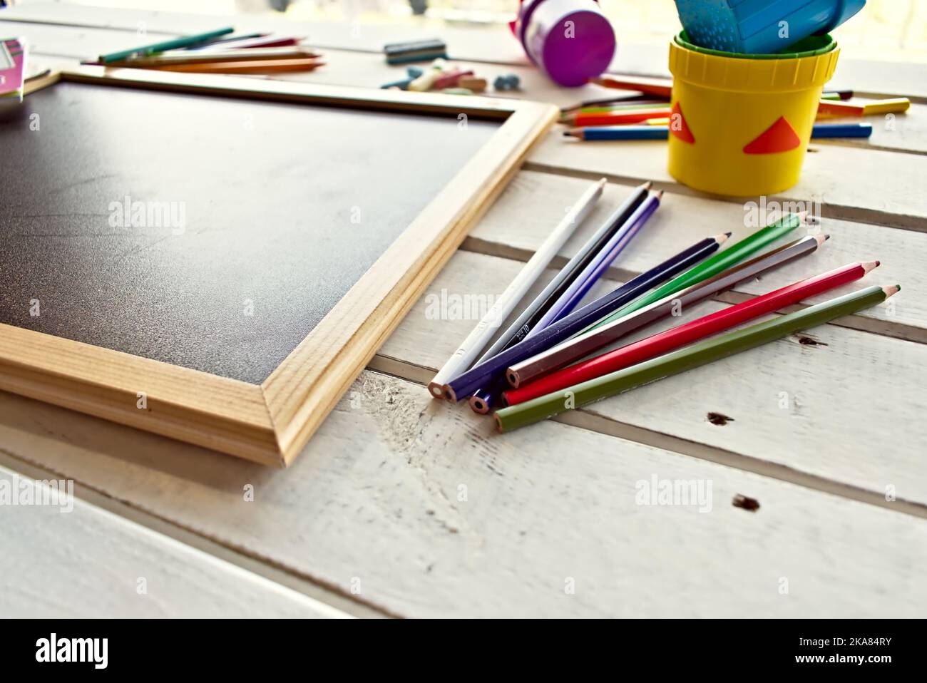 A wooden table with a chalkboard and colorful pencils Stock Photo - Alamy
