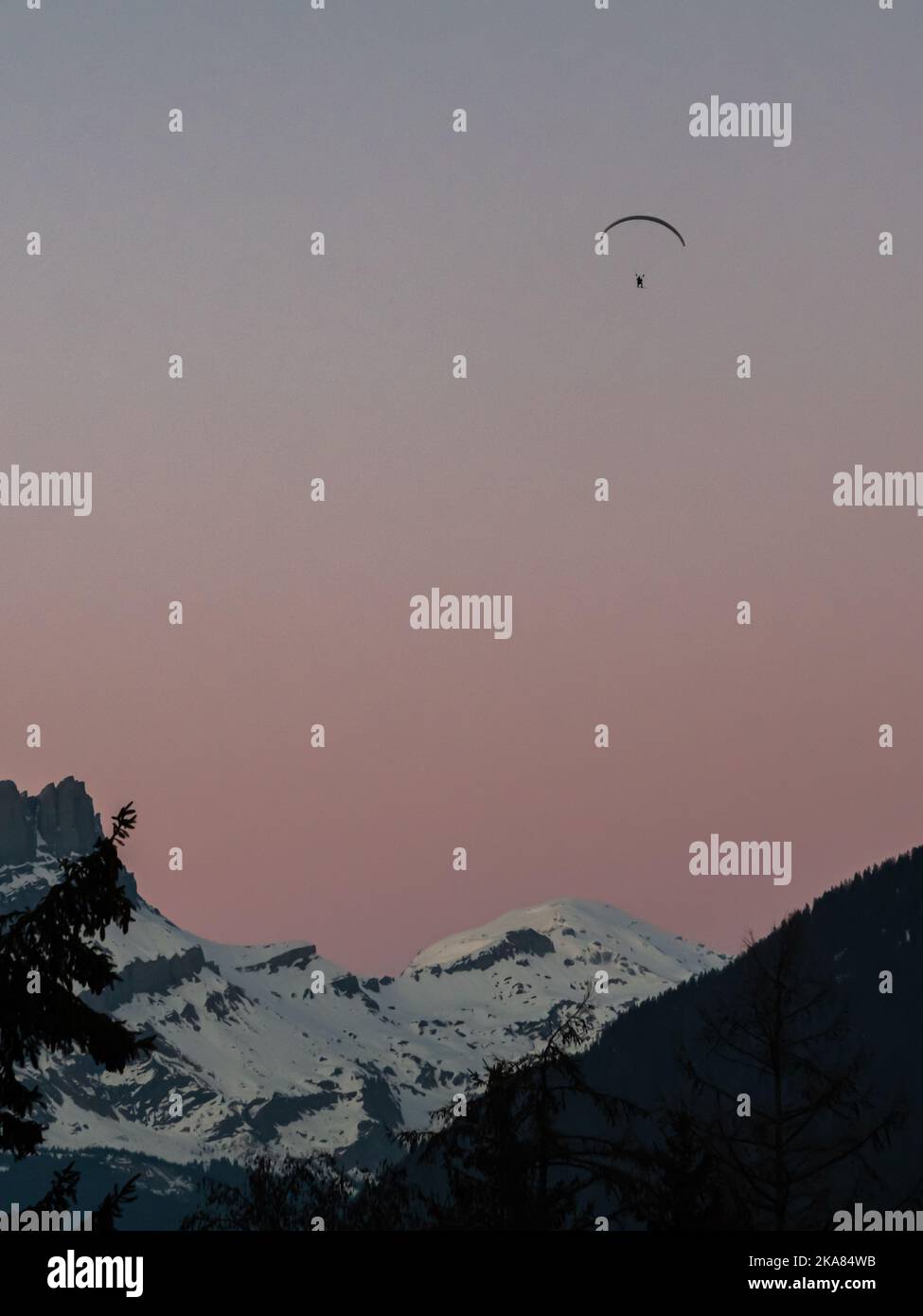 A vertical shot of the snow capped Mont Blanc and a paraglider against a sunset sky in France ...