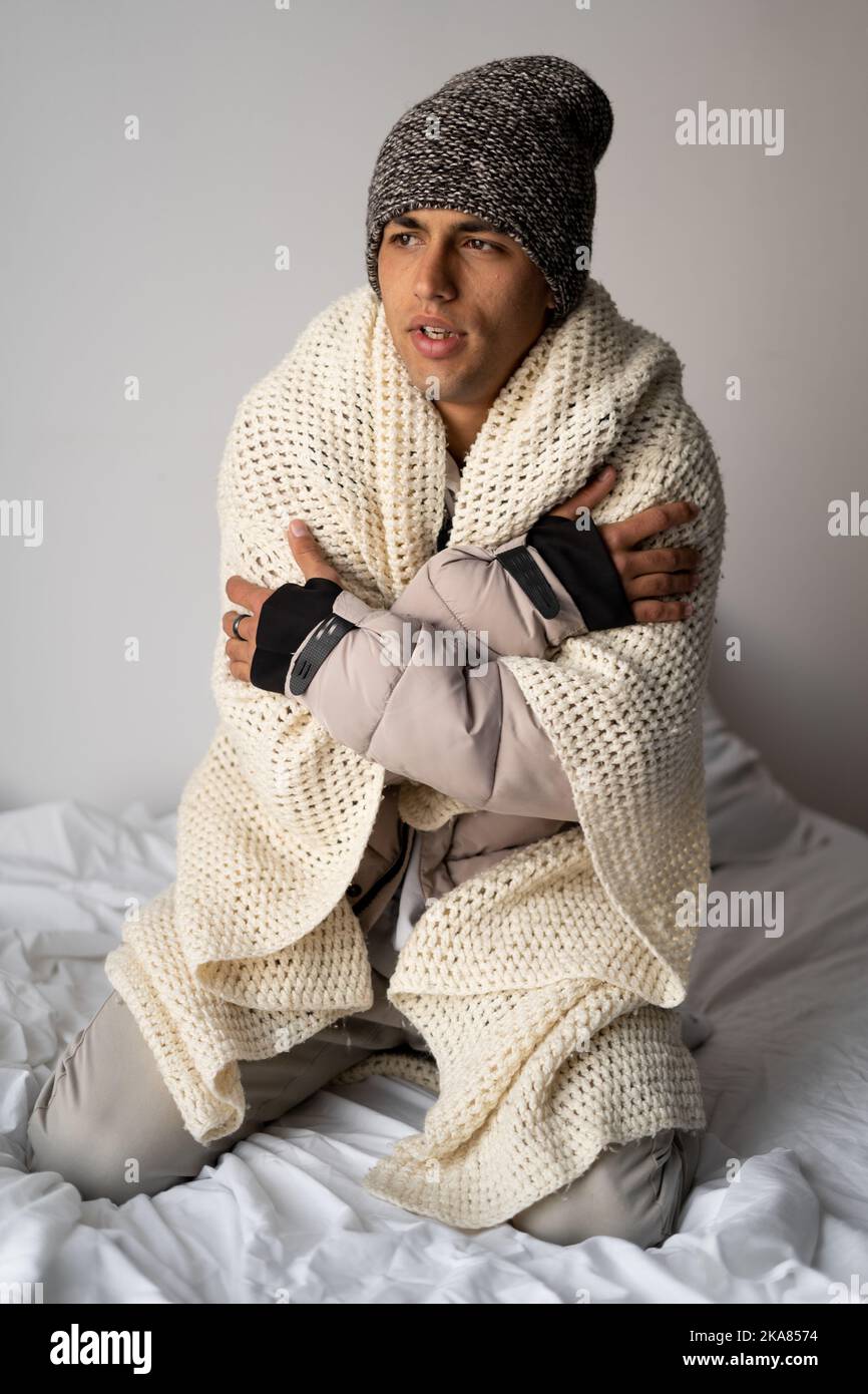 Young man warmly dressed is feeling cold, covered with warm blanket ...