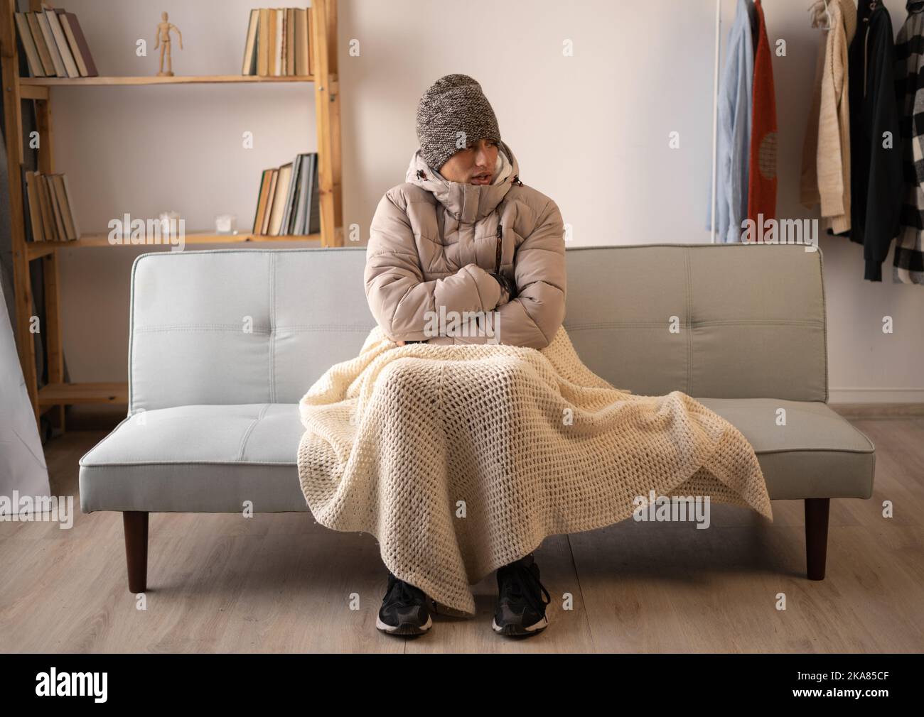 Unwell man in hat and blanket sit in cold living room suffer from heat ...