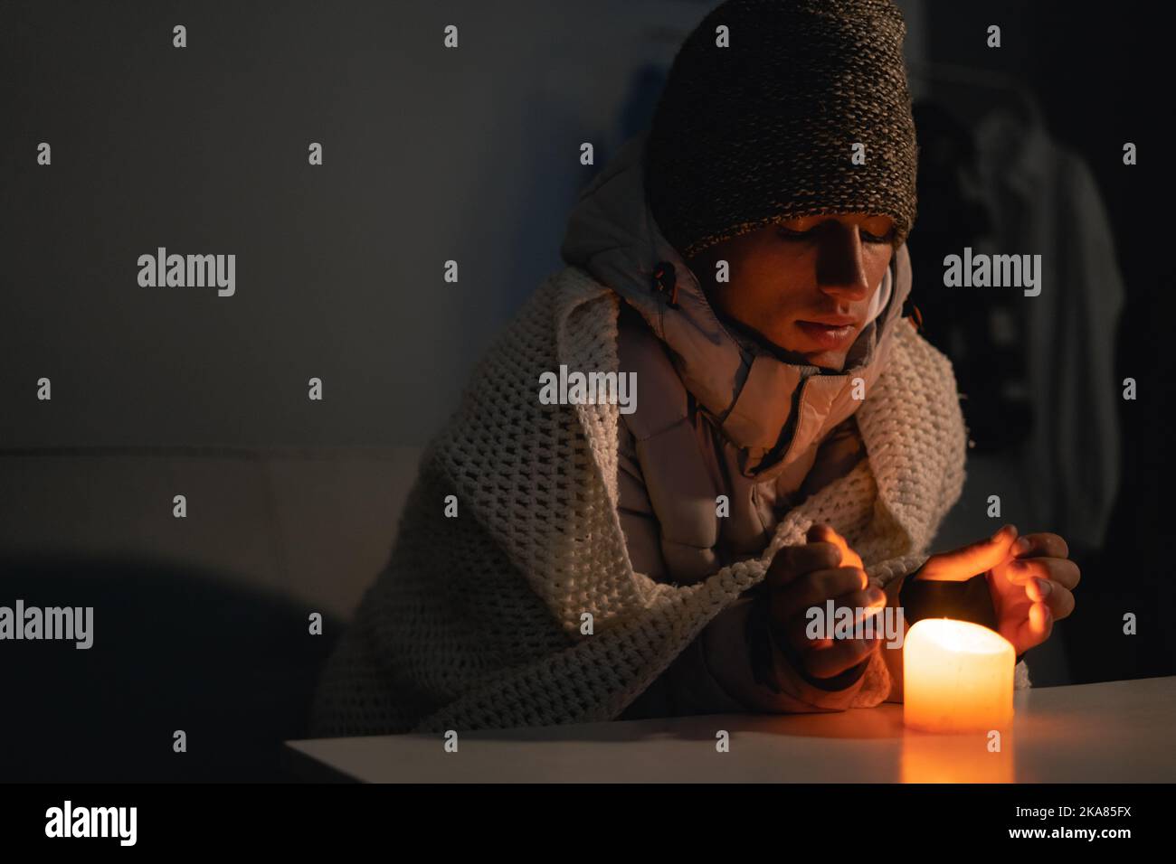 A young man dressed in a warm winter hat at home at a table and warms ...