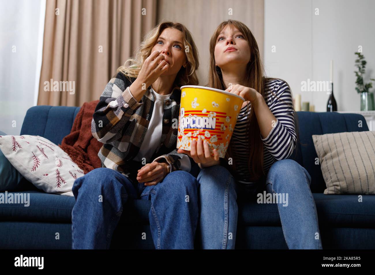 Two women of different ages eating popcorn are concentrated on watching ...