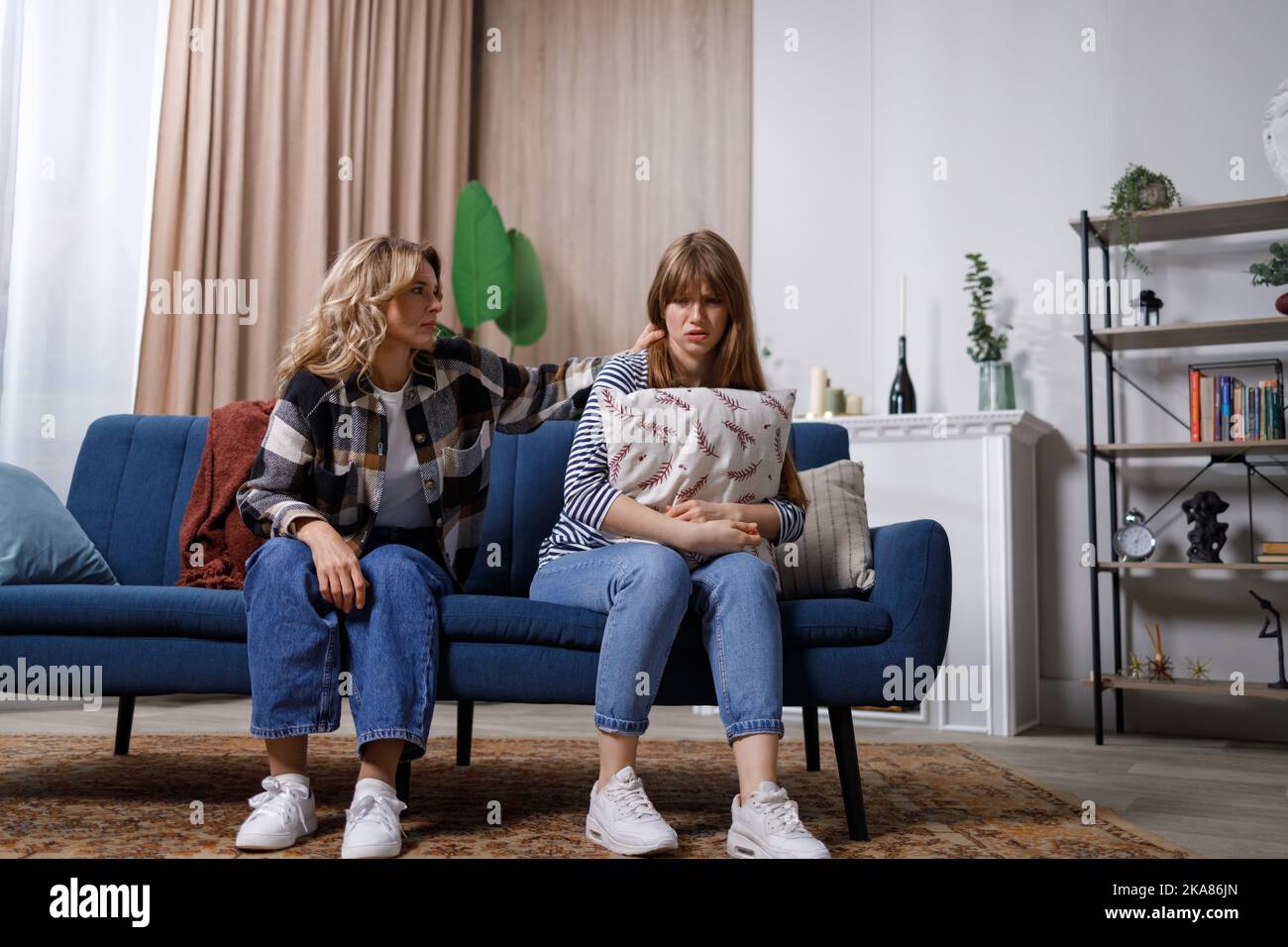 Mature woman sitting on a sofa is trying to calm her daughter who is ...