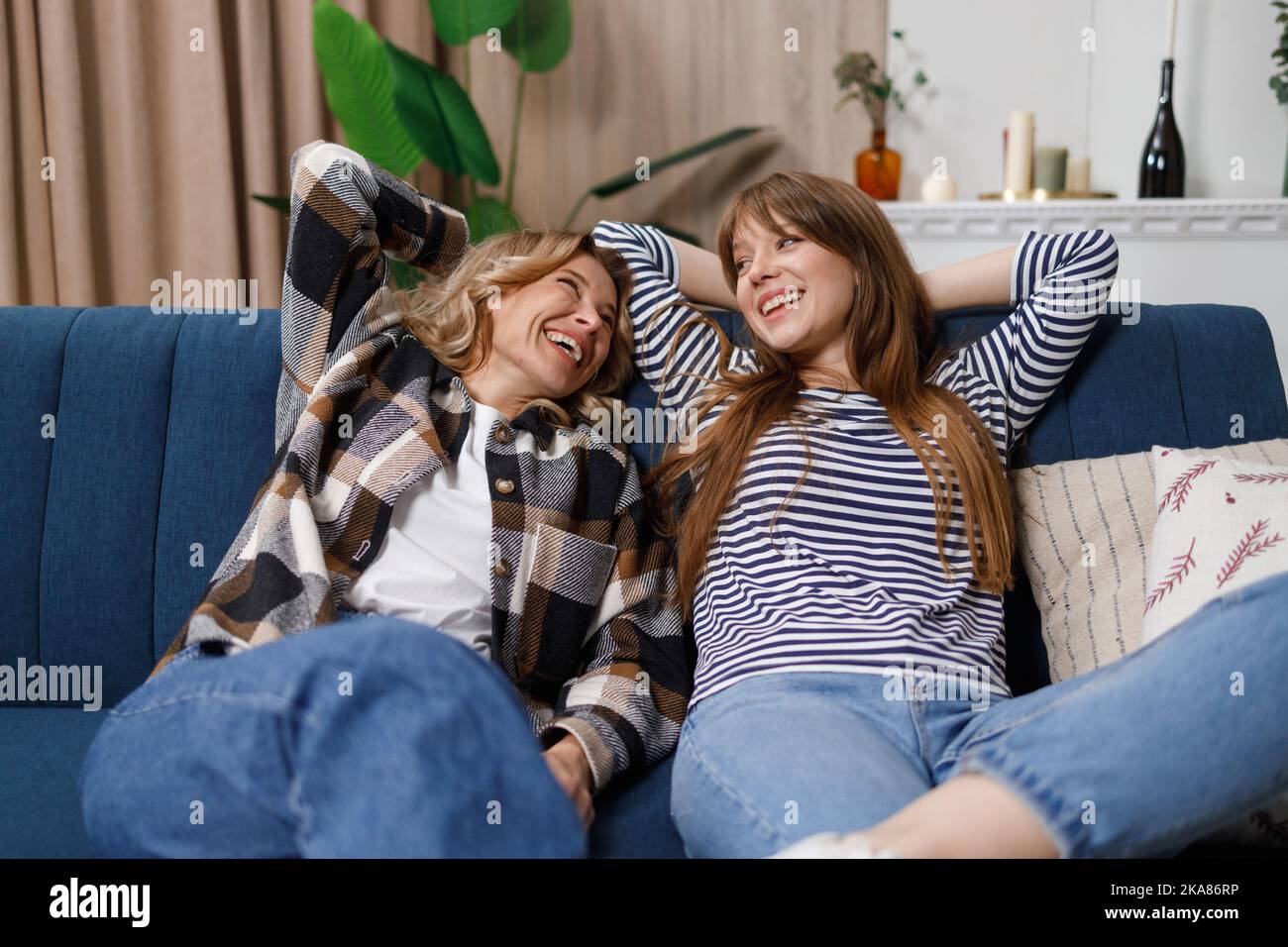 Lazy mother and daughter are lying on the sofa with their hands above ...