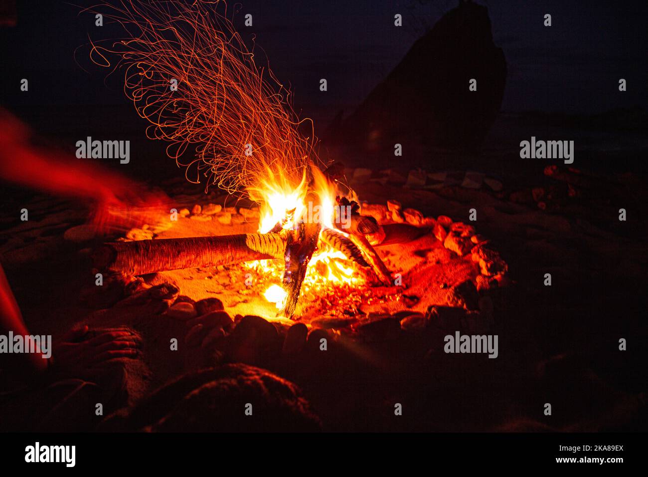 A vertical shot of a small camp fire on the beach by the water and a ...
