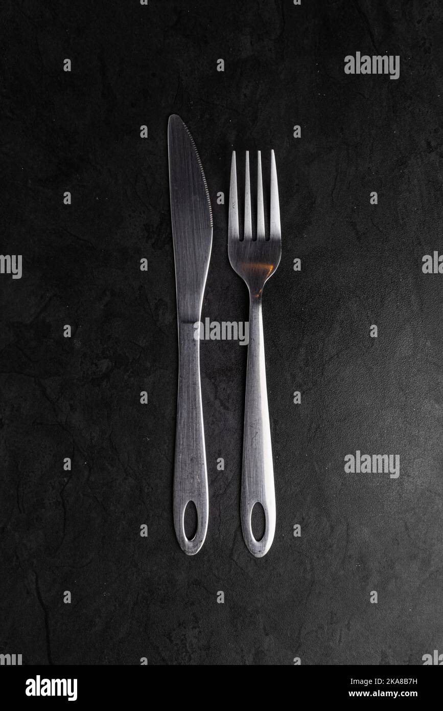 A vertical shot of old stainless steel knife and fork on a black ...