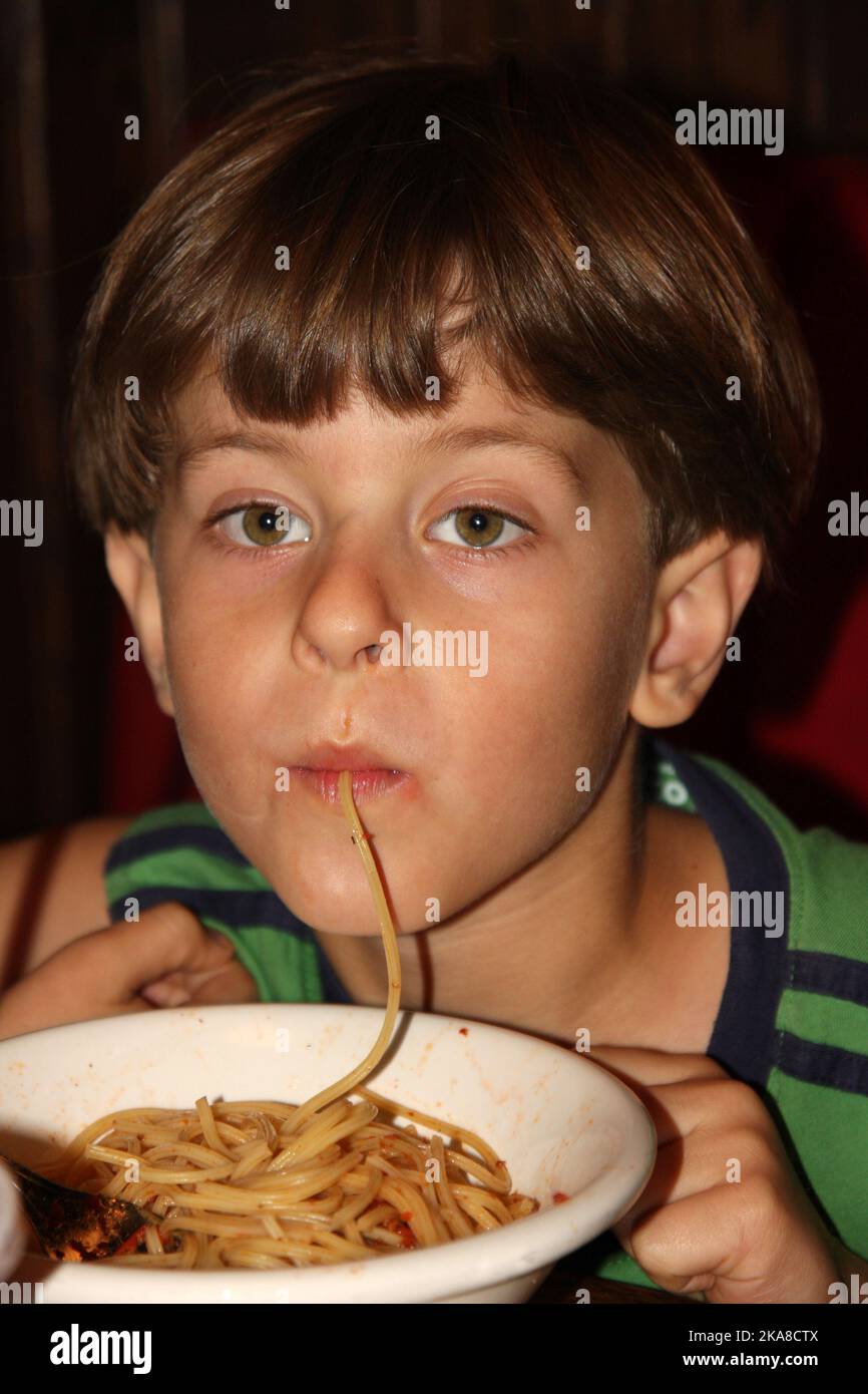 A young boy eating his spaghetti, sucking in one noodle at a time as he ...