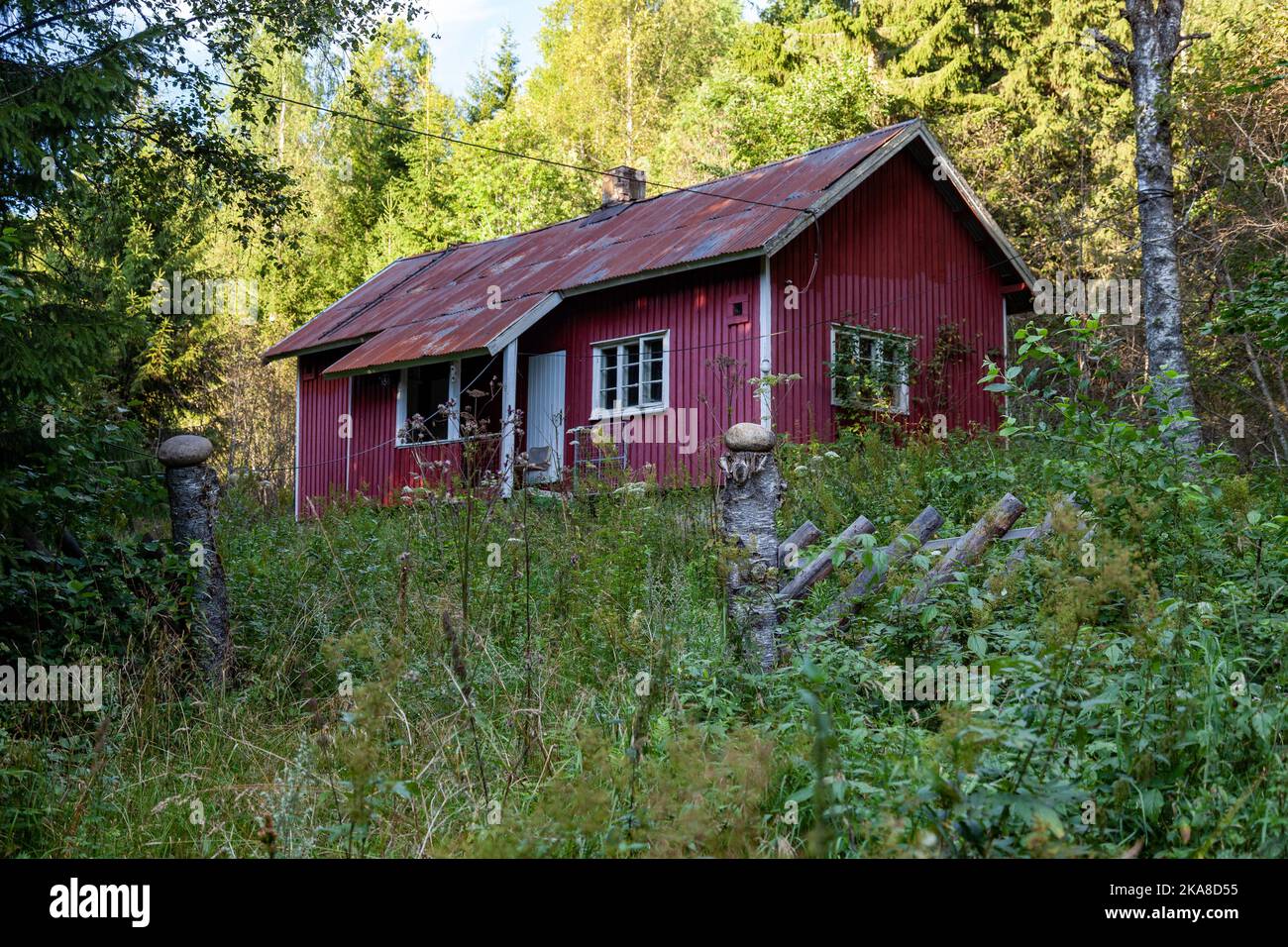 A rural wooden building painted red in a forested area under the bright ...