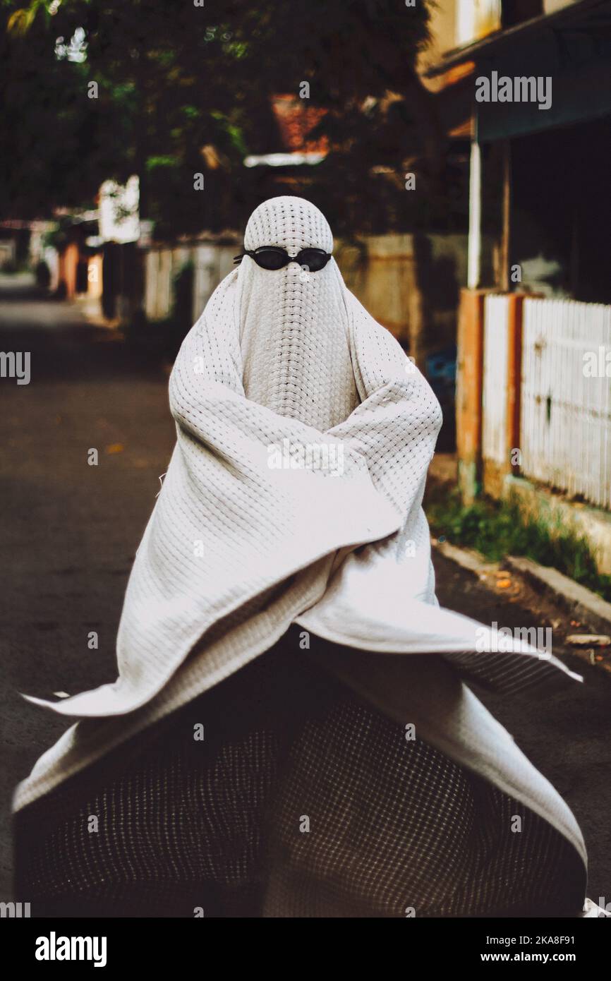 A vertical shot of human with black glasses in white ghost costume ...