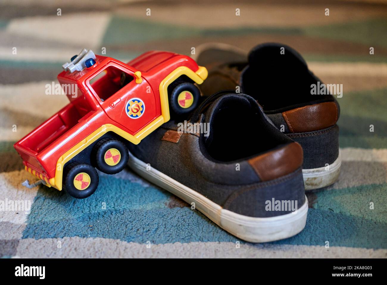 A plastic toy Fireman Sam vehicle laying on a pair of shoes on a carpet ...