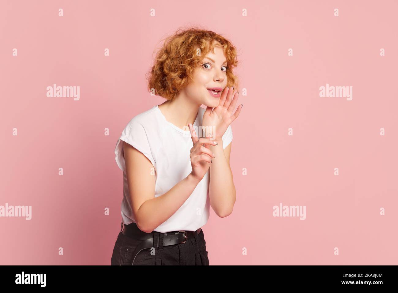 Secrets. Beautiful young redheaded woman whispering isolated on pink ...