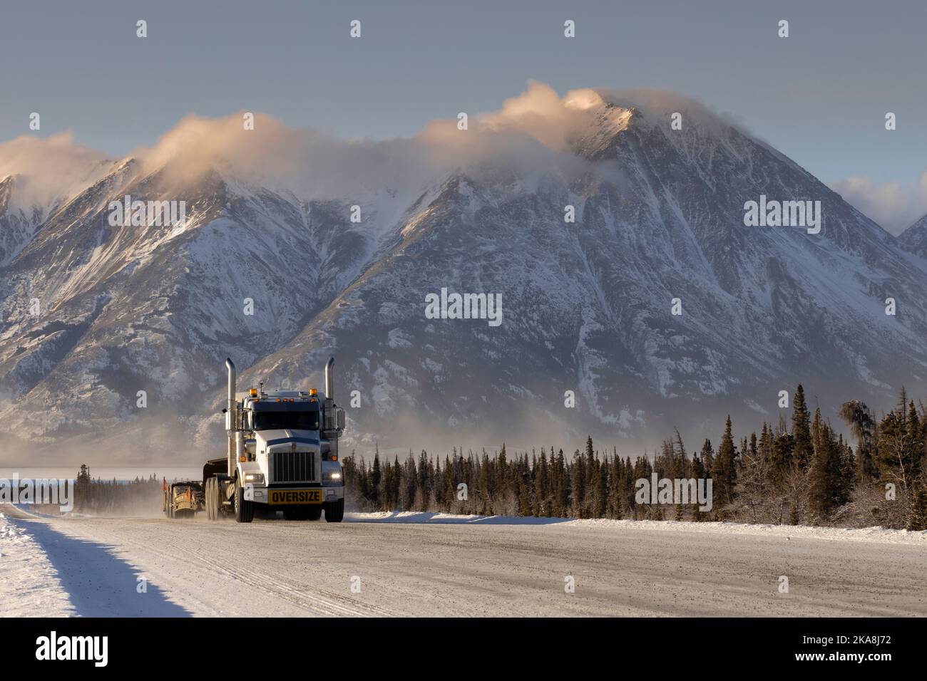 An oversize load truck in the road with forests and snowy mountains in ...