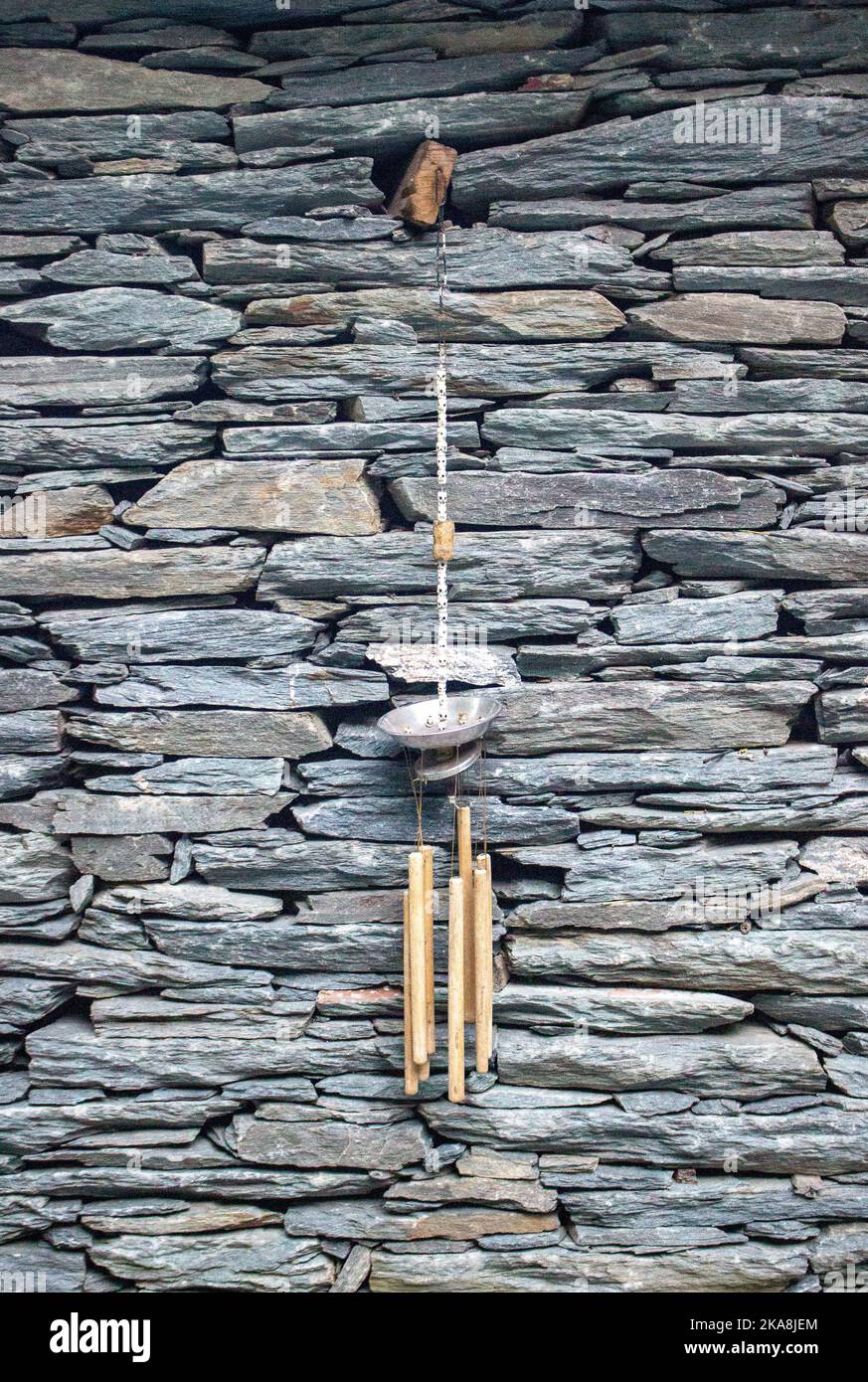 A vertical shot of a traditional wind chime hanging from a stone wall ...
