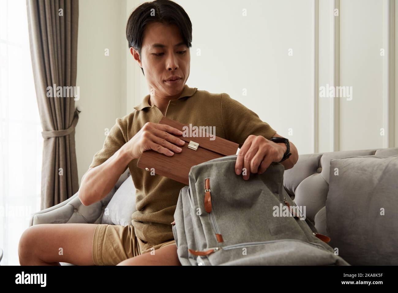 Serious young man putting planner in backpack when leaving house for ...