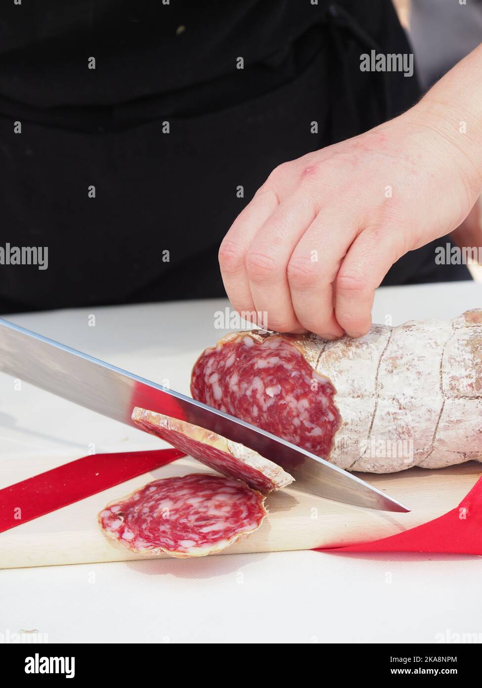 catering and waiting staff hand with knife slicing salami ham in a ...