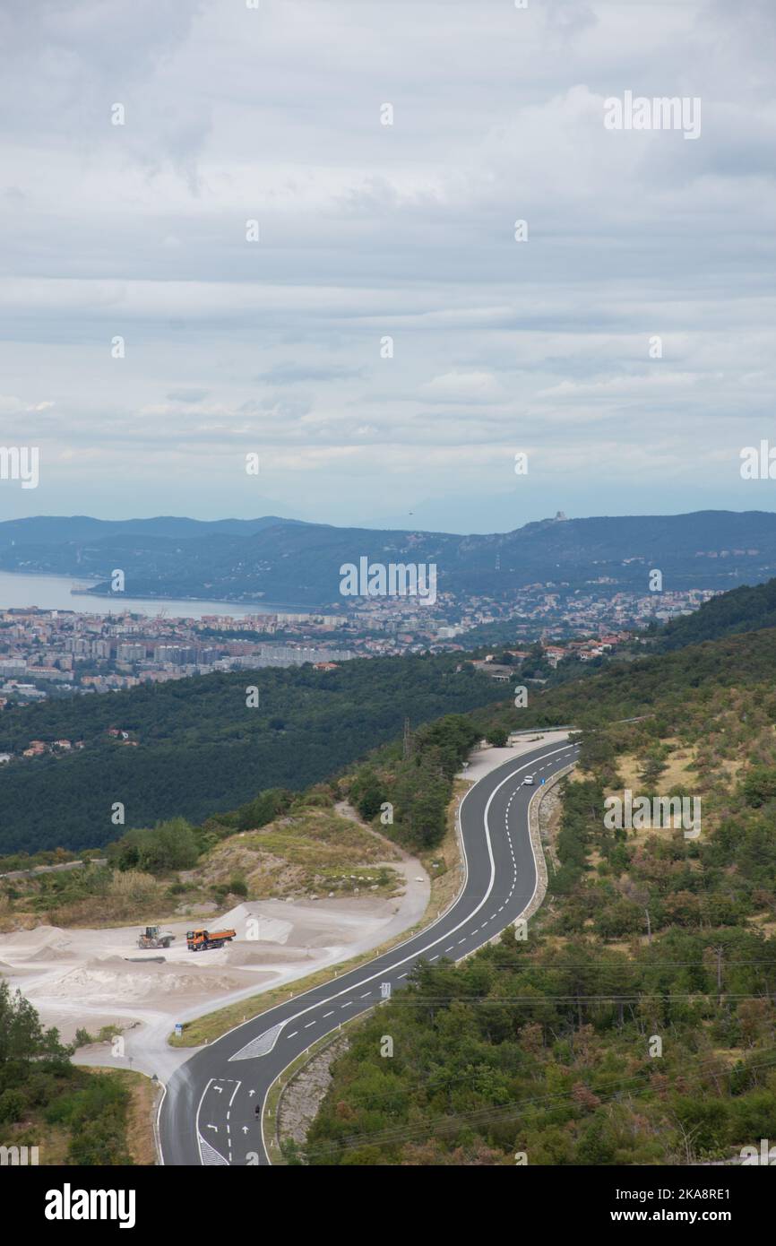 A vertical shot of an asphalt highway against green hills on a gloomy ...