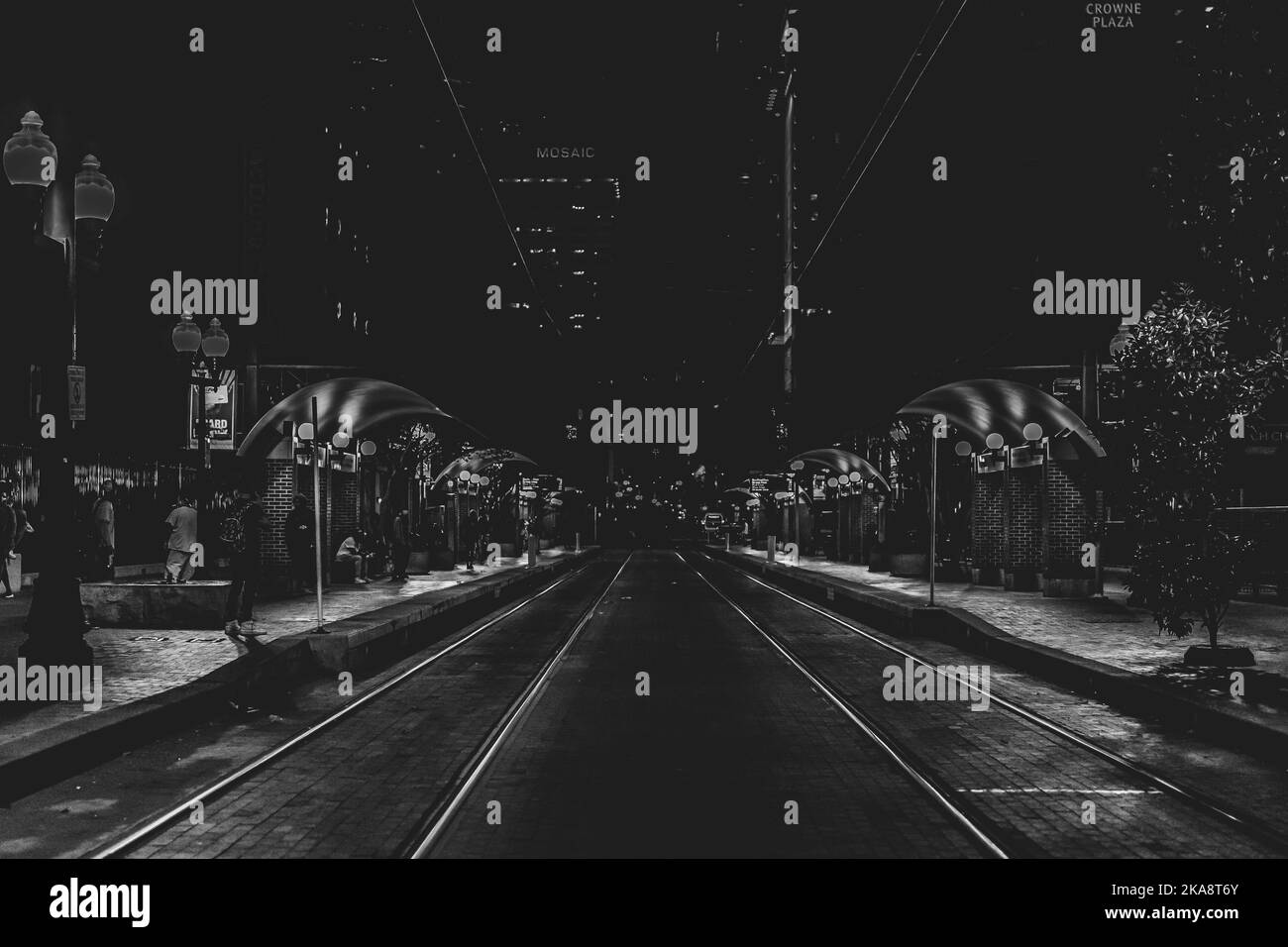 A grayscale shot of dark night view of a road with tram lines with ...