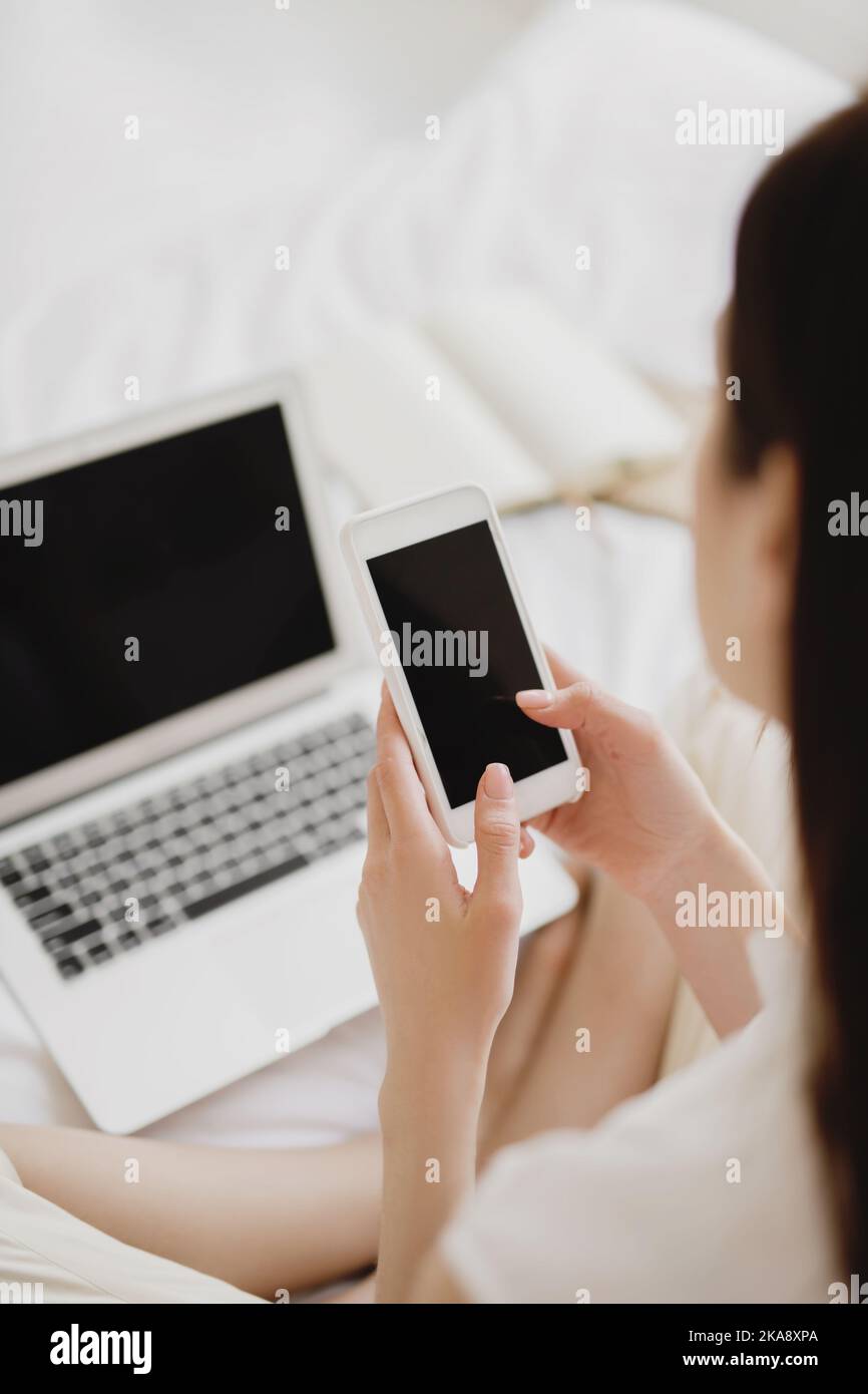 Back view of young woman using smartphone and laptop with blank screen ...