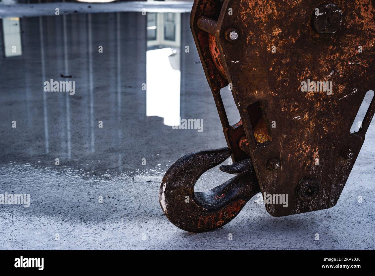 A rusted metal crane hook on the ground by a water puddle Stock Photo ...