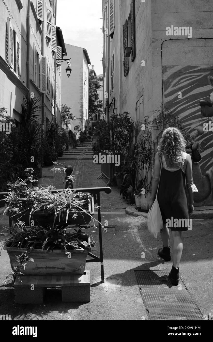 A grayscale shot of a beautiful young woman walking in the narrow ...