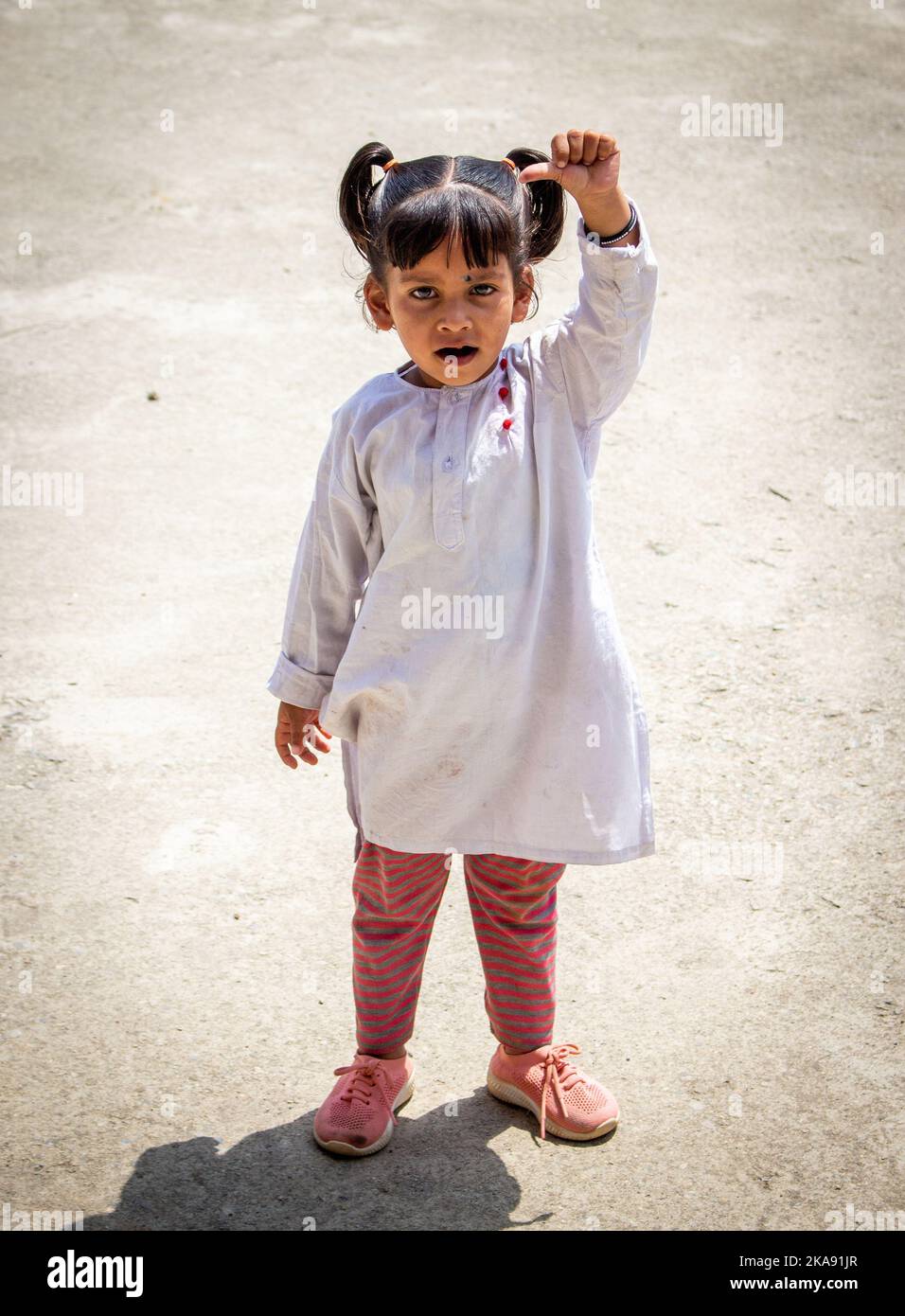 A closeup of a young Indian girl with pigtails wearing a white dress ...