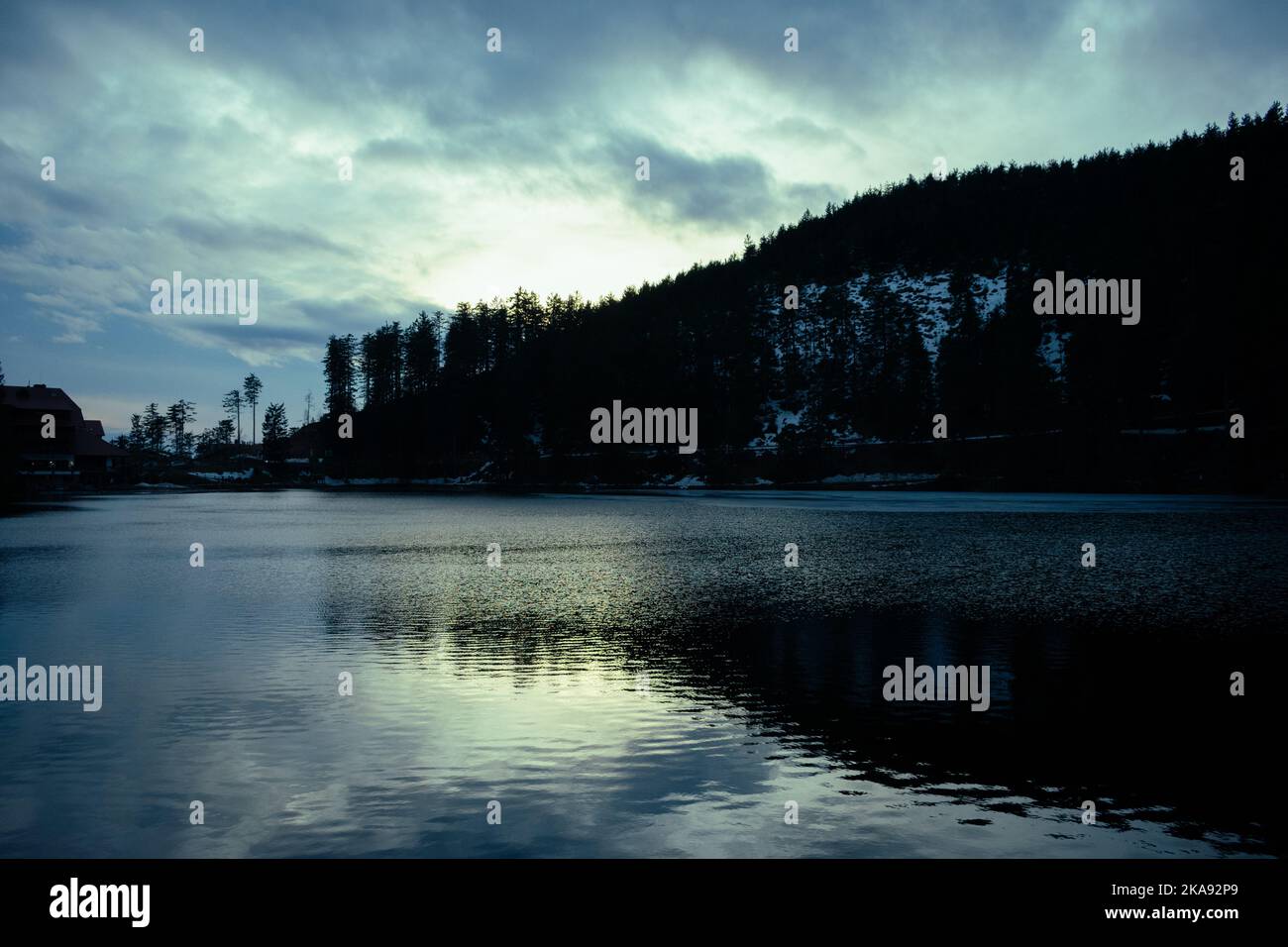A beautiful landscape with a lake and a forested snowy mountain under a ...