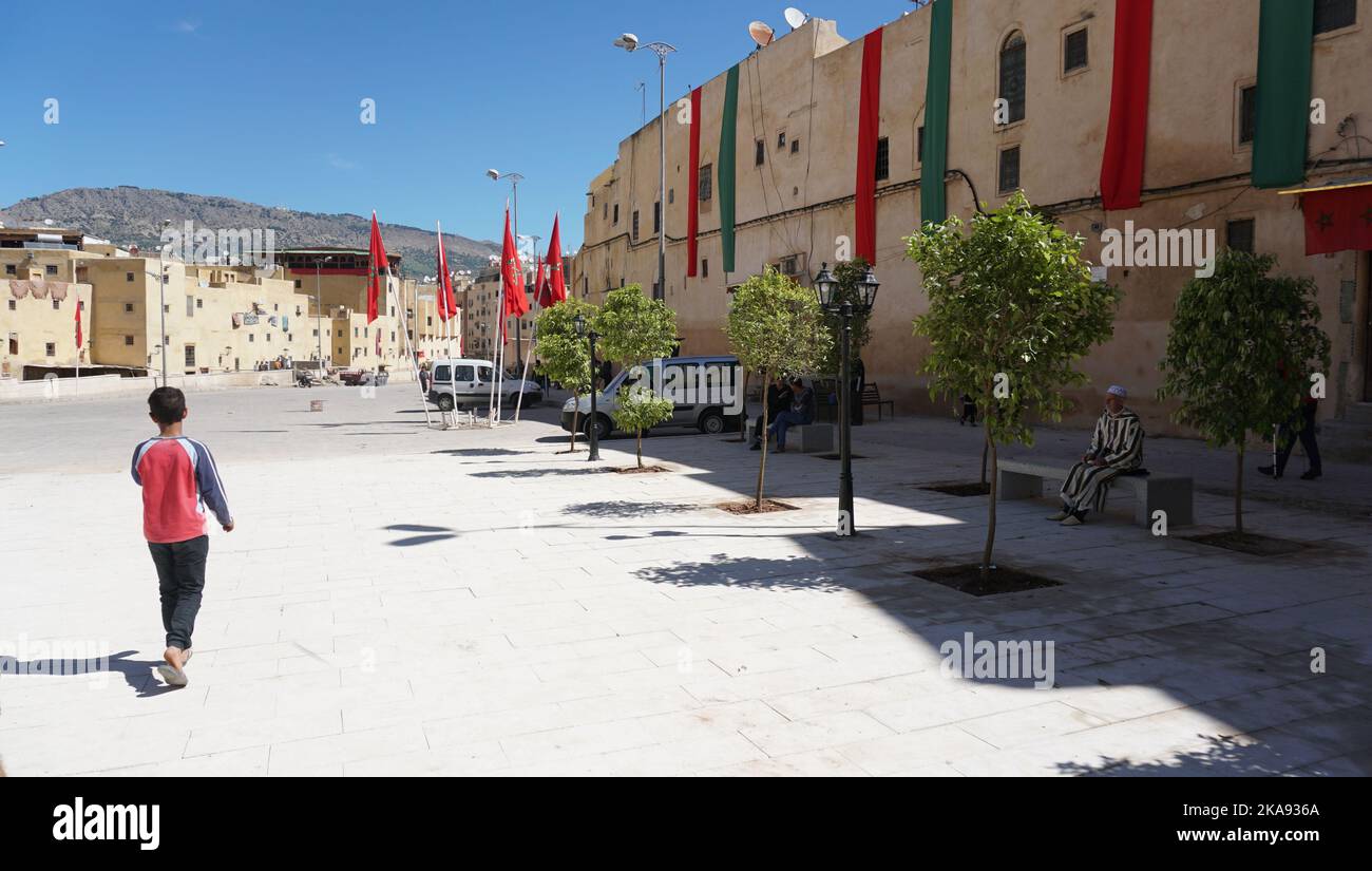 A young boy walking on an empty plaza with flags in Fes on Morocco ...