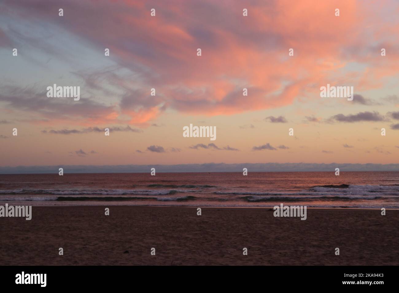 A scenic view of a tranquil sea reflecting the beautiful cloudy sunset ...