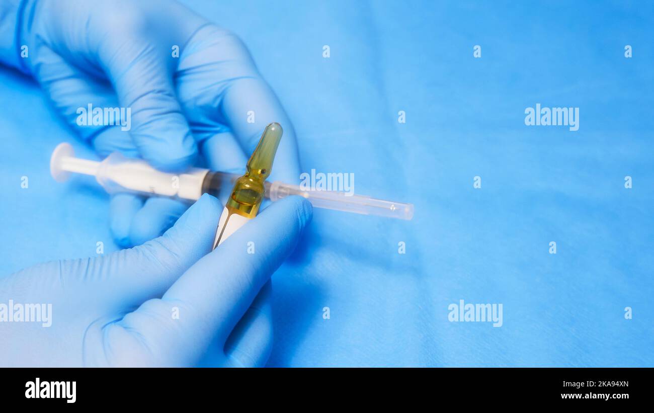 The nurse's hands in blue protective gloves hold an ampoule and a ...