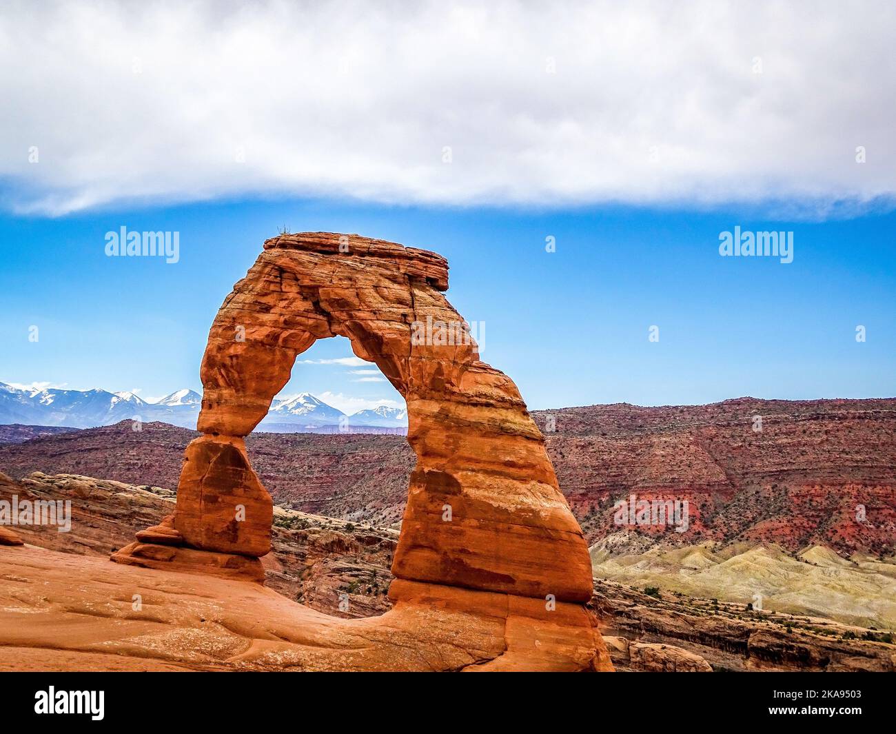 A red sandstone arch with cloudy sky in the background in Arches ...