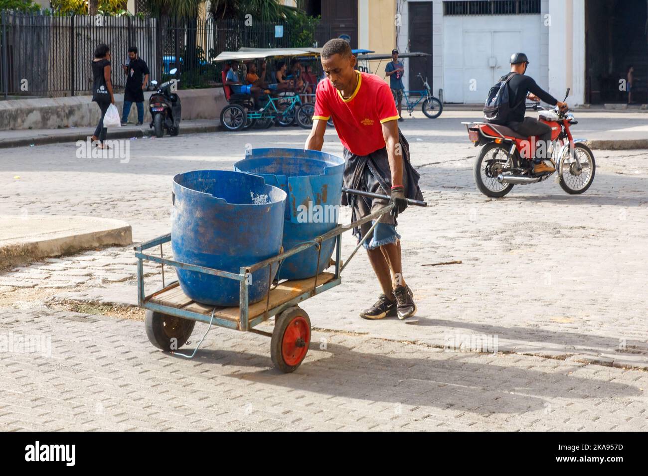 A Cuban Afro-Caribbean man pushes a cart with two plastic tanks. He is ...