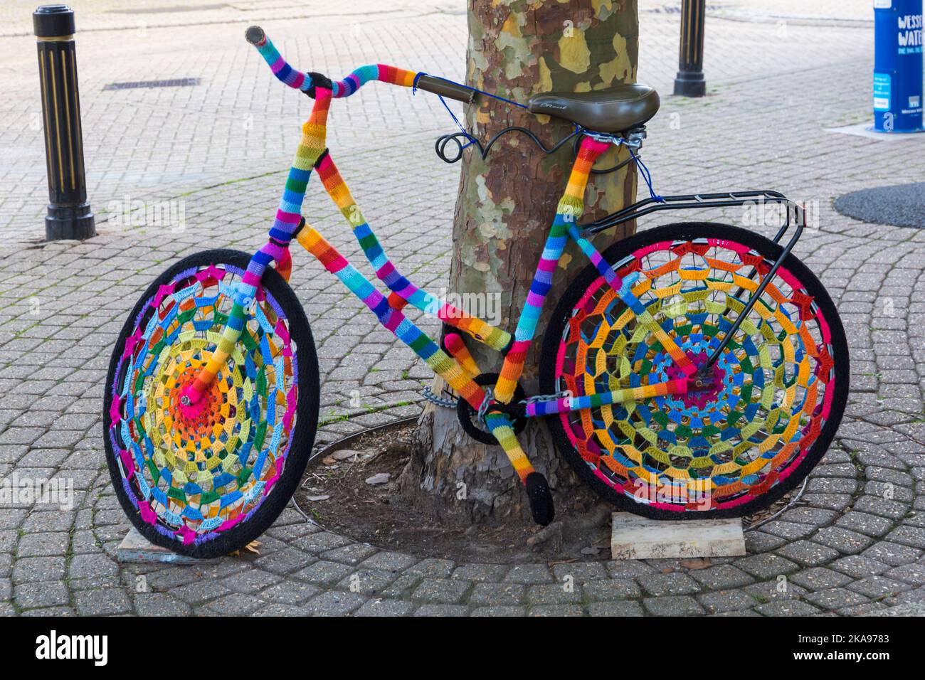 Colourful yarn bombing bike, yarn bomb crochet crocheted bike against tree in Weymouth, Dorset ...