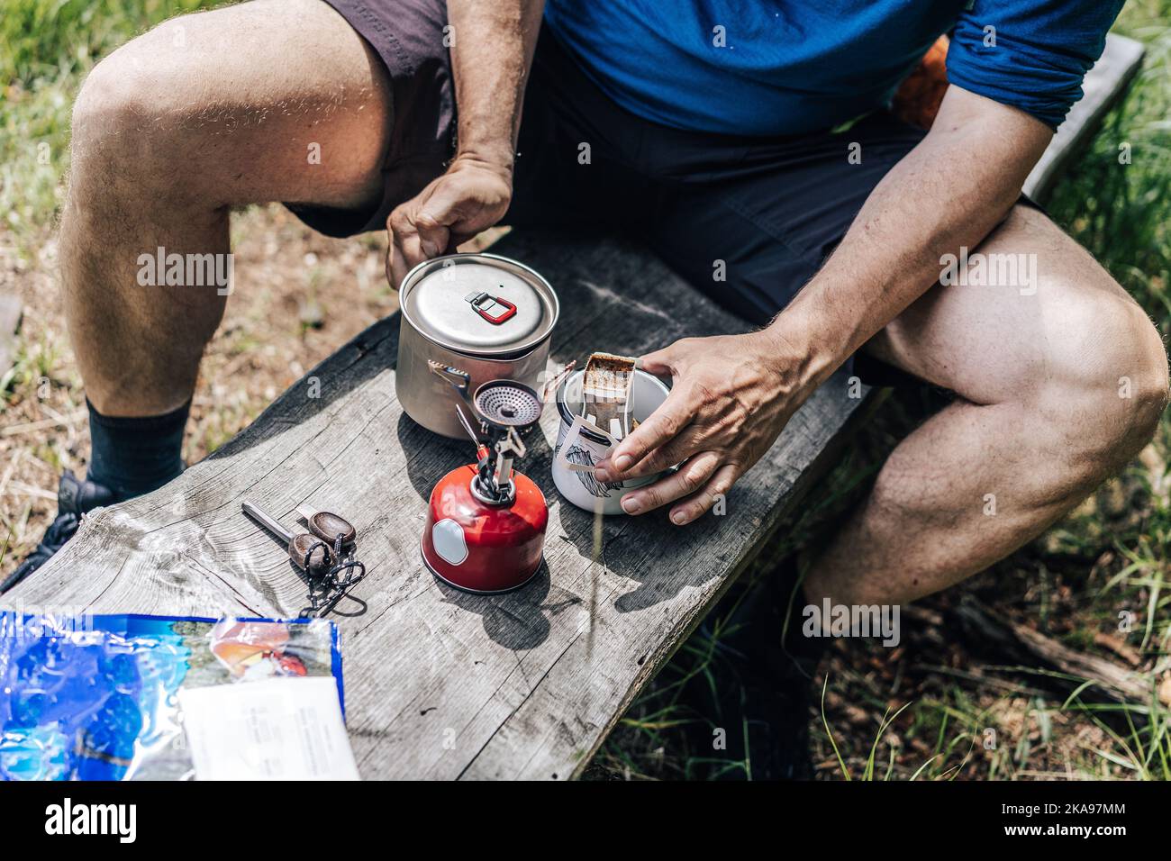 A man boiling water on an outdoor camnping stove and preparing coffee ...