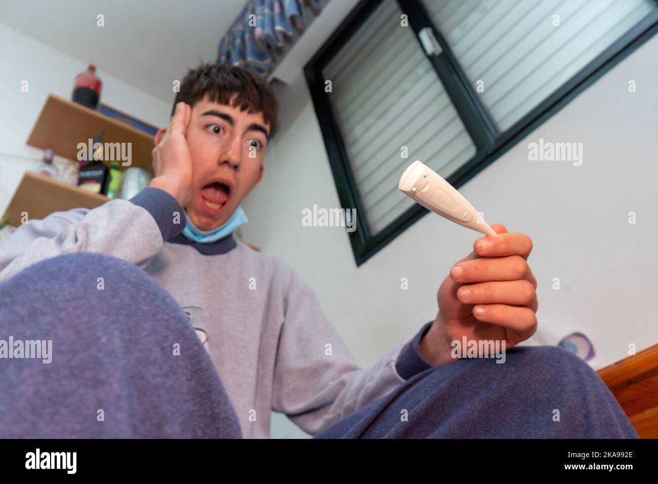 A sick Caucasian guy shocked when looking at a thermometer at home ...