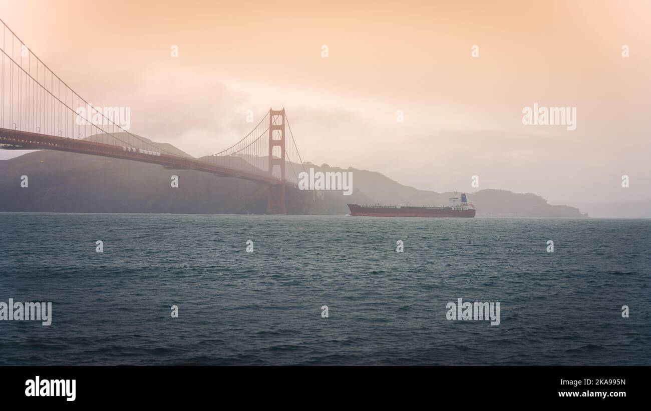 A sunset view of a container ship crossing the Golden Gate Bridge, San ...