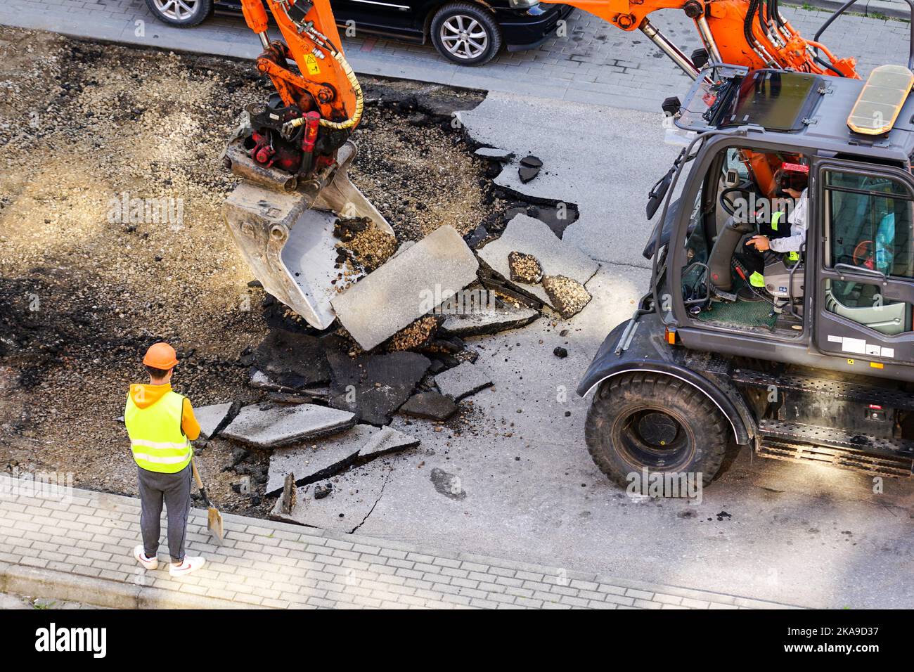 An excavator breaks up the old asphalt layer with a bucket during ...