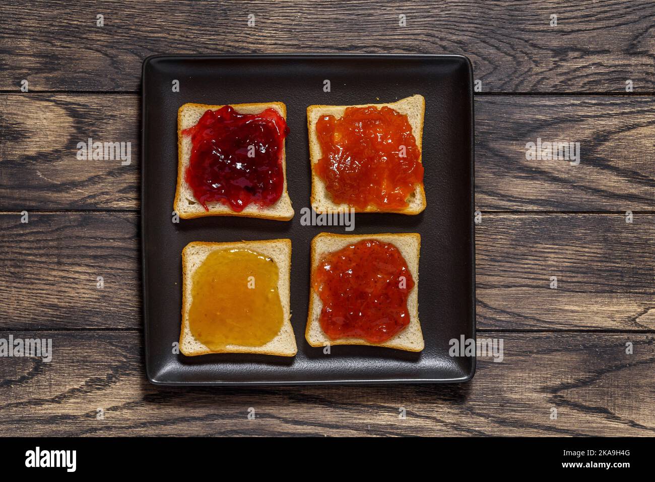 Toasted bread with different jams on square black plate on table top ...