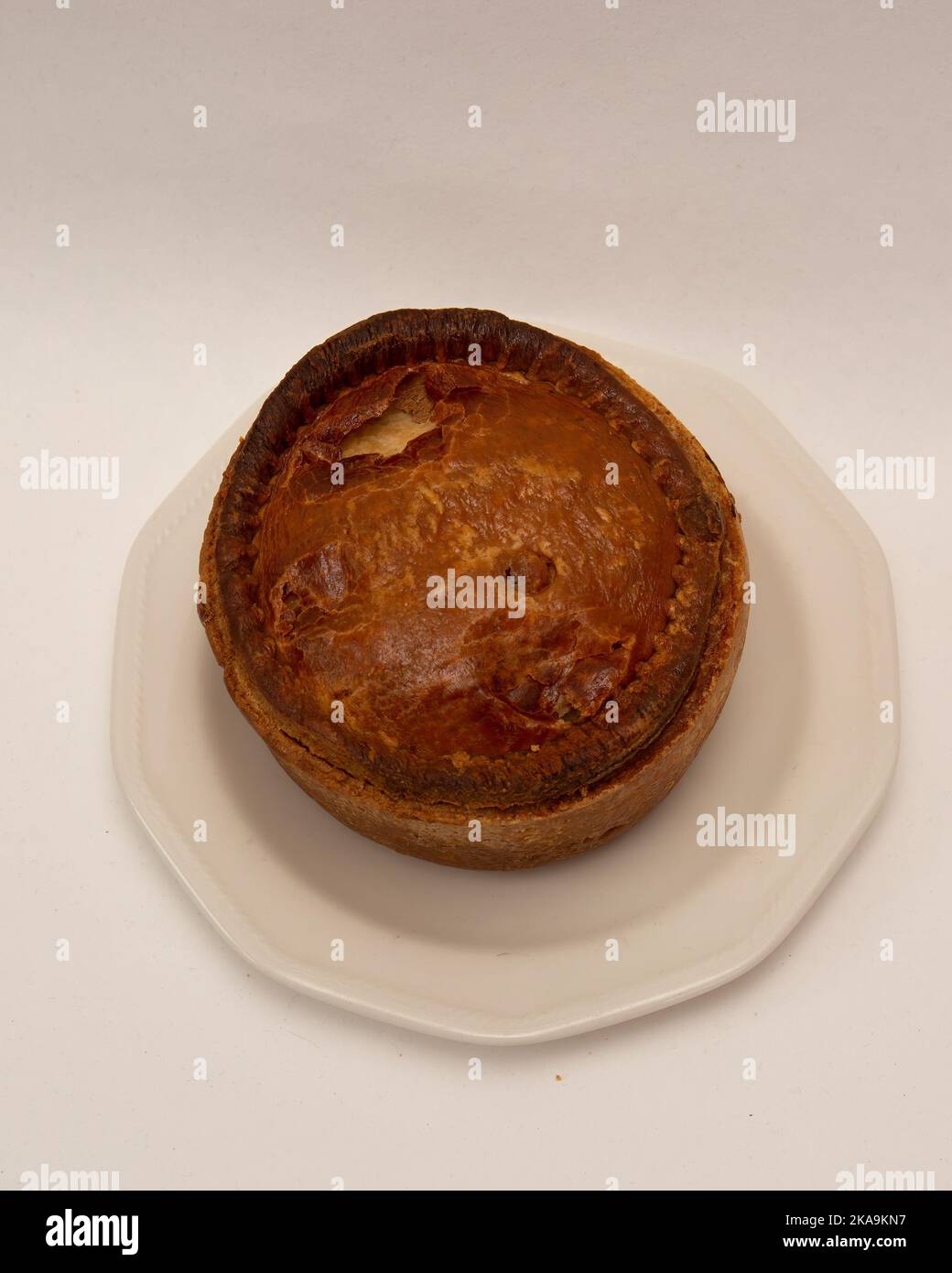 A vertical view of Tasty British crusty pork pie on plate isolated on ...