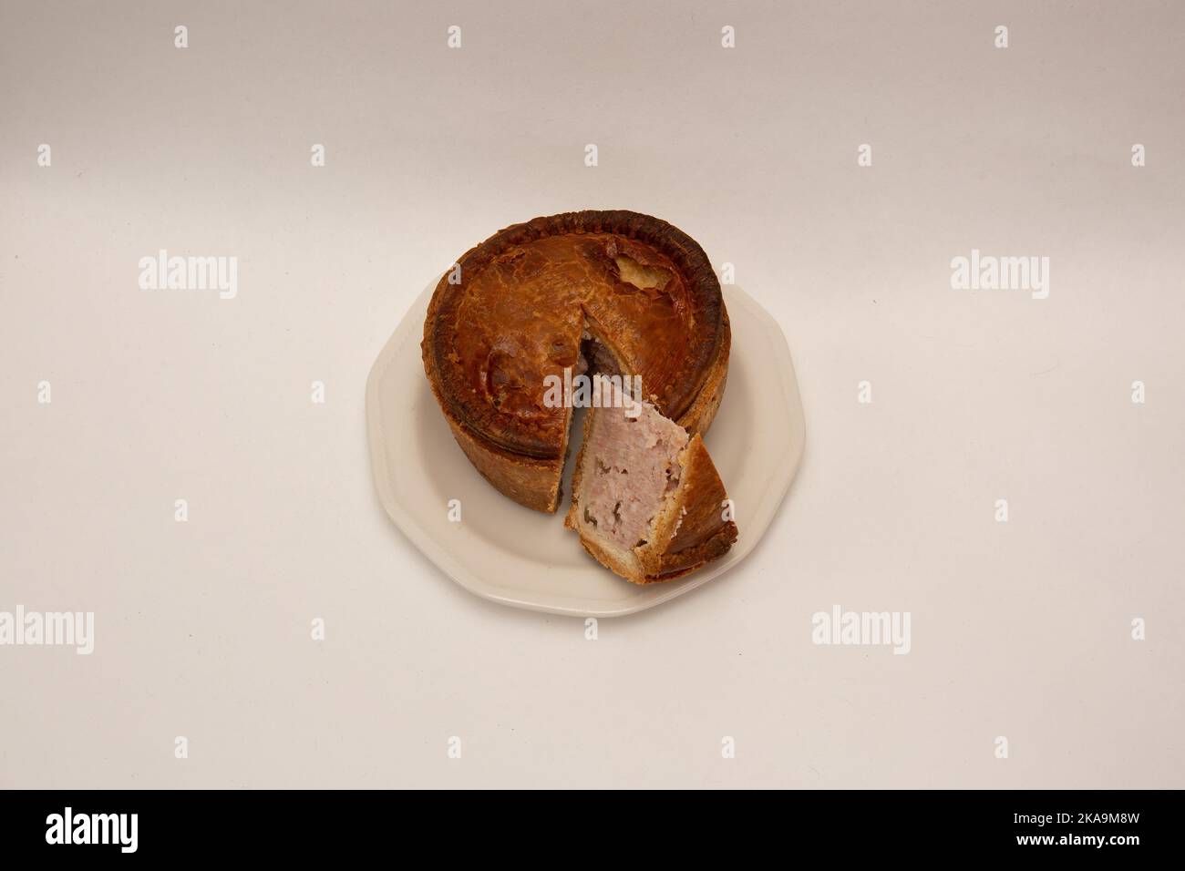 Tasty British crusty pork pie with slice cut ready on plate isolated on ...