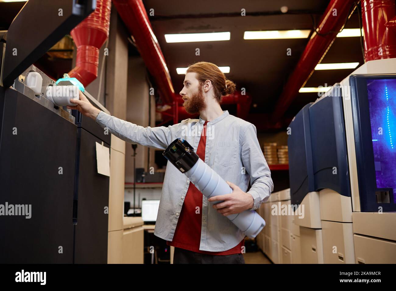 Side view portrait of young man filling ink tanks of industrial ...